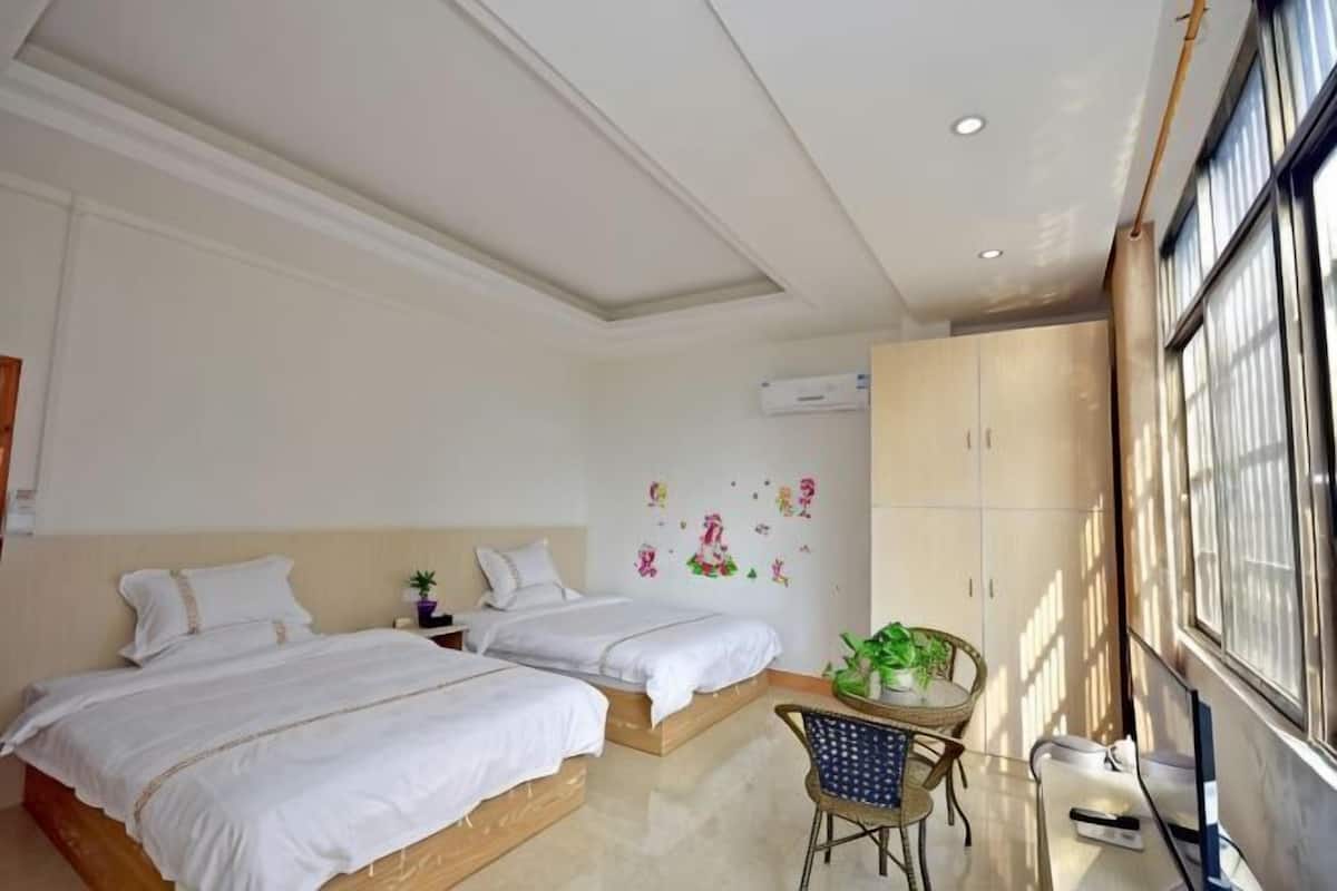 Quarto com duas camas, uma mesinha com uma planta, uma cadeira e uma janela com vista.