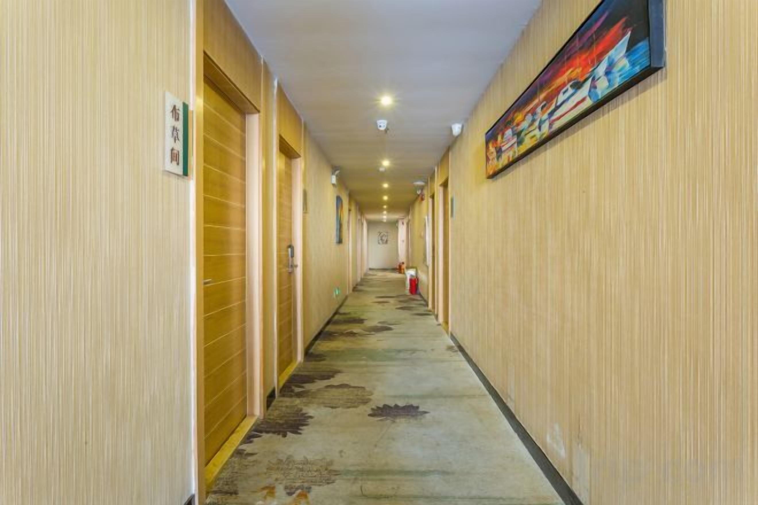 Corredor de hotel com portas em ambos os lados, um extintor de incêndio e um quadro na parede.