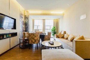 Quarto de hotel com televisão de tela plana, um sofá, uma mesa de jantar com cadeiras e uma mesa redonda pequena.