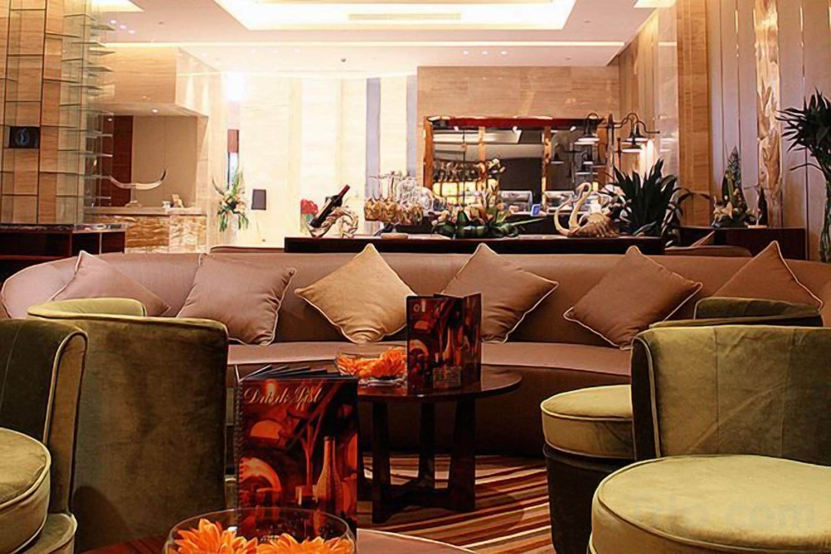 Um hall de hotel moderno com um sofá, cadeiras, uma mesa de centro e um objeto decorativo.