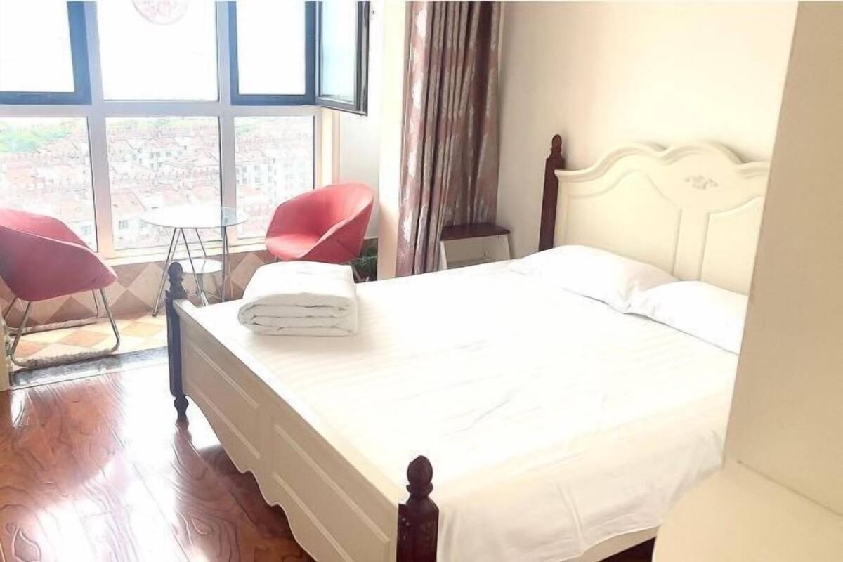 Quarto de hotel com cama, uma cadeira, uma mesinha e janela com vista para edifícios.