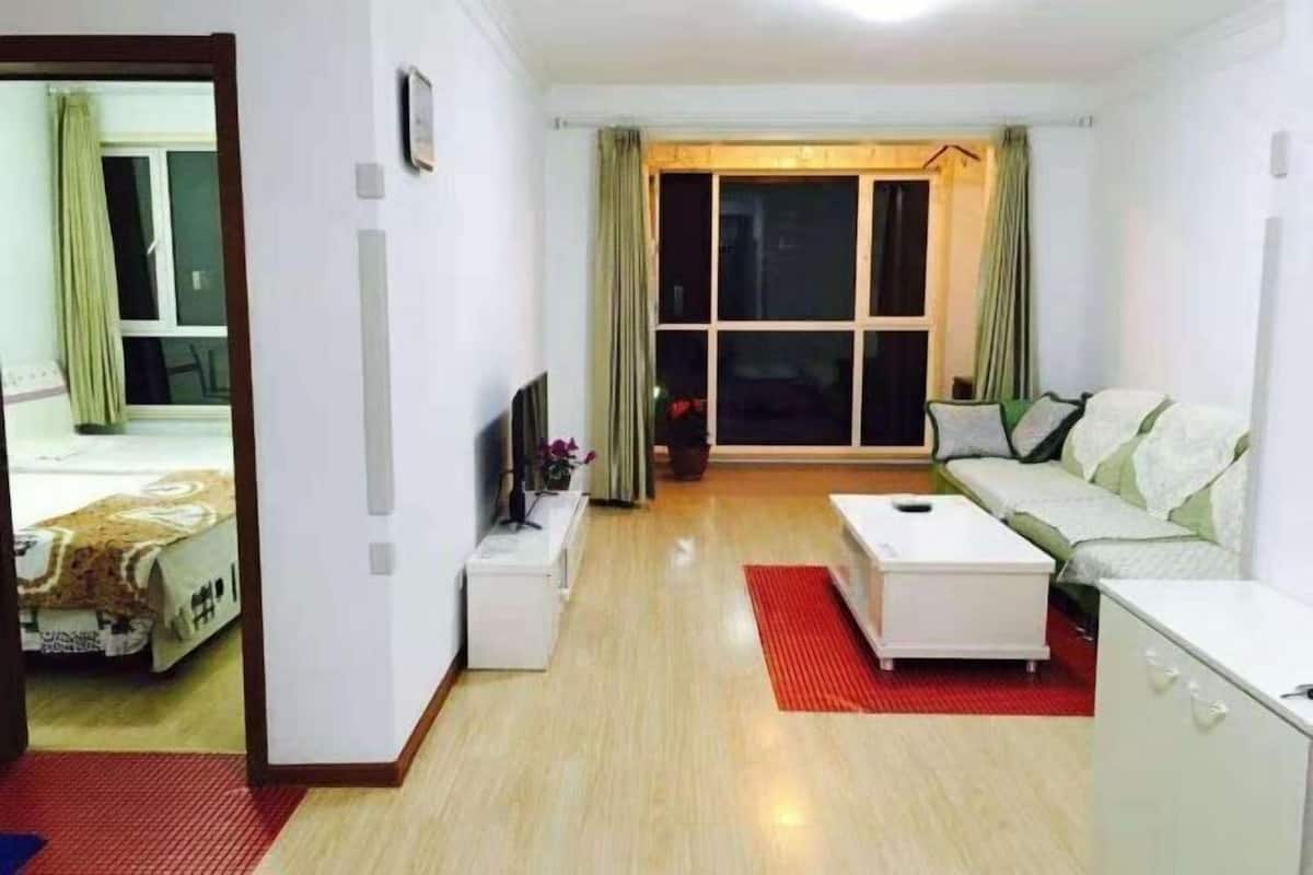 Sala de estar moderna com sofá, mesa de centro e televisão. Há uma porta de correr que dá para uma varanda.