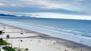 Uma praia com pessoas e veículos, céu claro e montanhas ao longe.