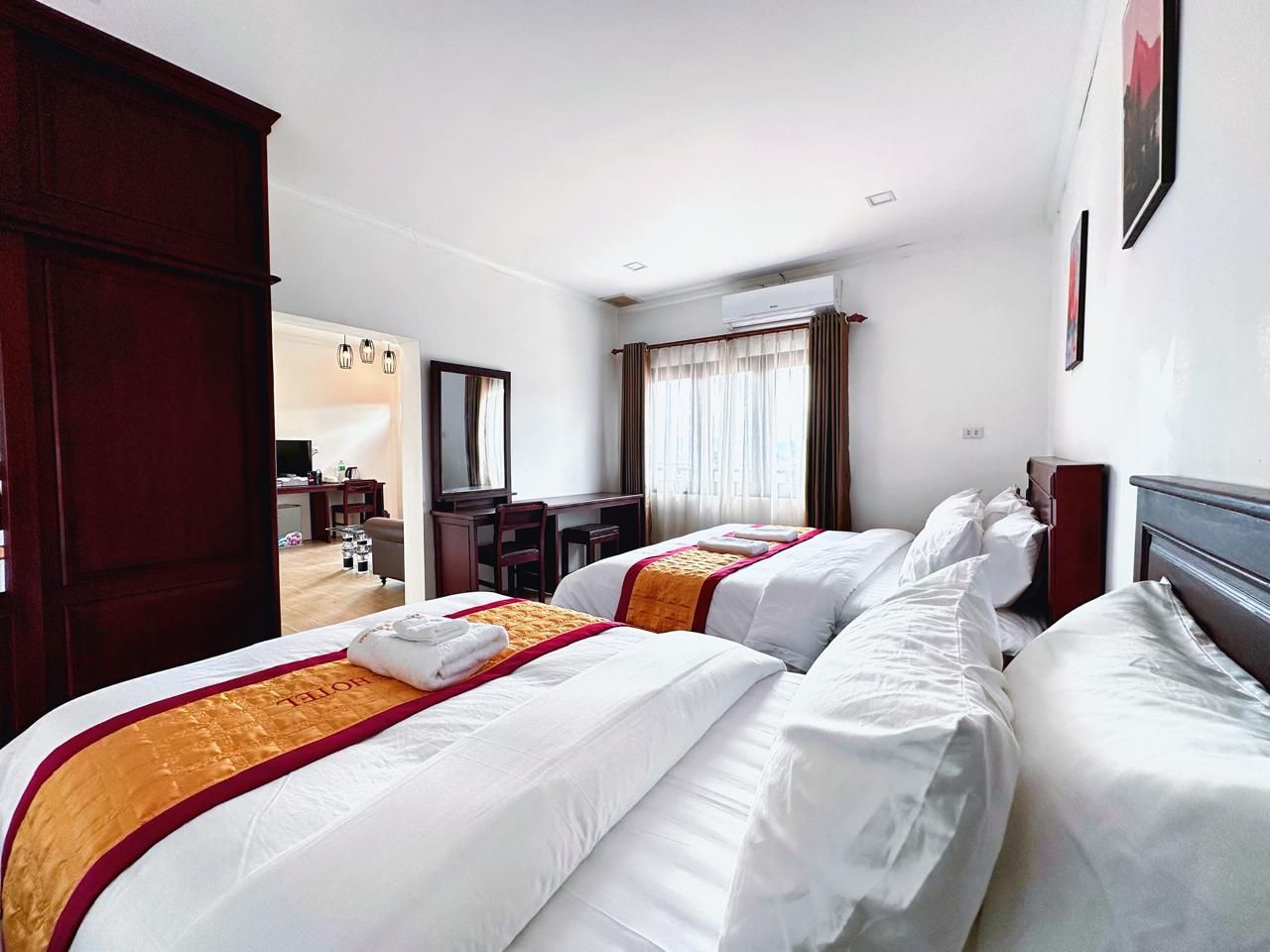 Quarto de hotel com duas camas, uma escrivaninha, uma cadeira e um guarda-roupa.