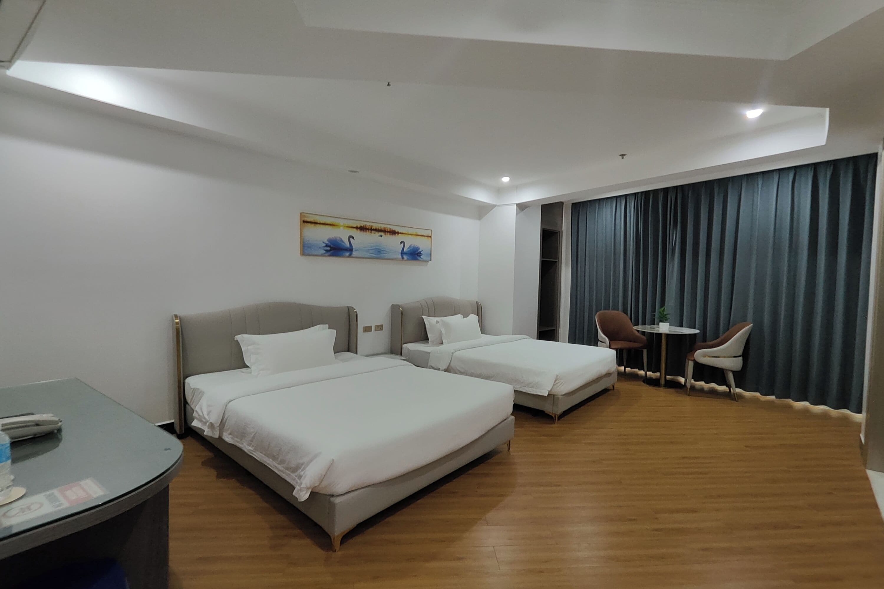 Quarto de hotel com duas camas, uma mesinha com cadeiras e um quadro na parede.