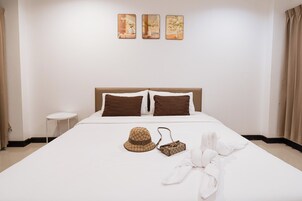 Quarto de hotel com cama, almofadas, um chapéu, uma bolsa e uma toalha.