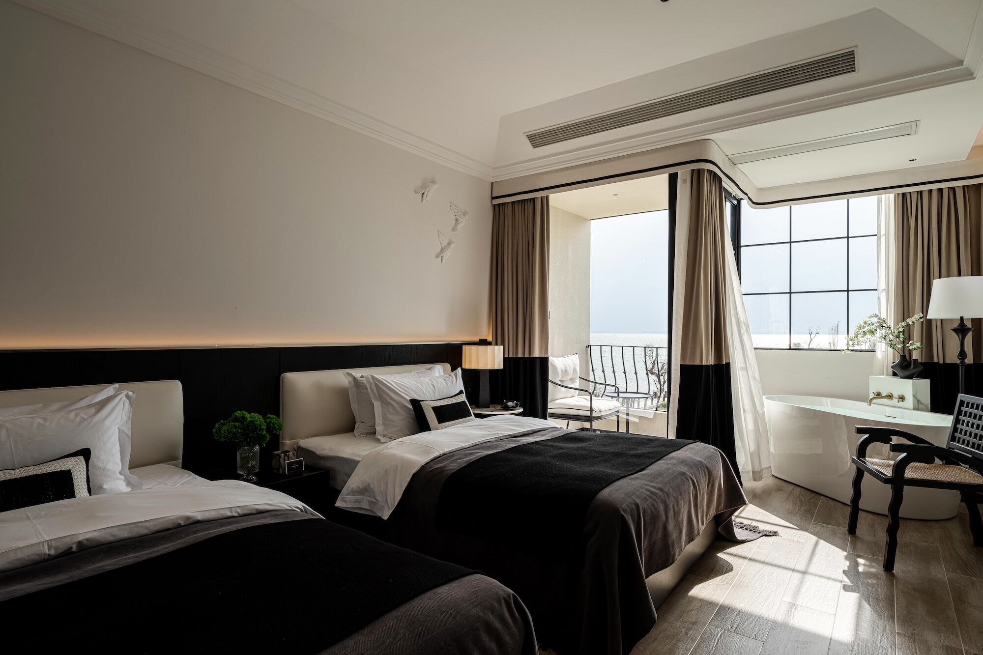 Quarto de hotel com duas camas, uma escrivaninha, uma cadeira e vista para o mar.
