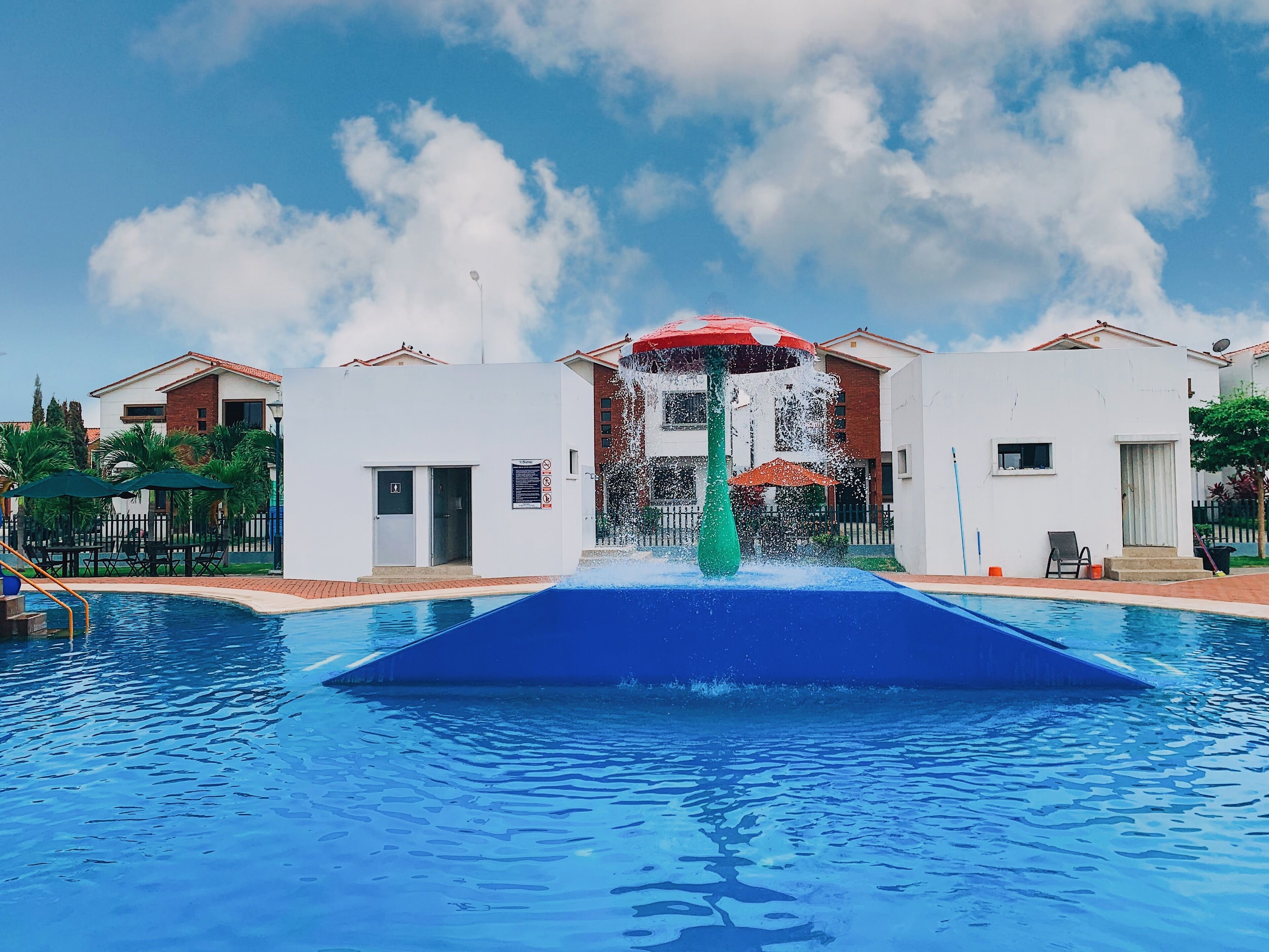 Piscina com um recurso de fonte, rodeada por edifícios com fachada branca e telhados de telhas vermelhas.