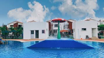 Piscina com um recurso de fonte, rodeada por edifícios com fachada branca e telhados de telhas vermelhas.