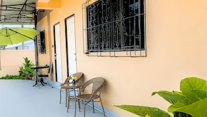 Uma área de estar coberta ao ar livre com cadeiras de vime, uma mesa e um guarda-sol verde.