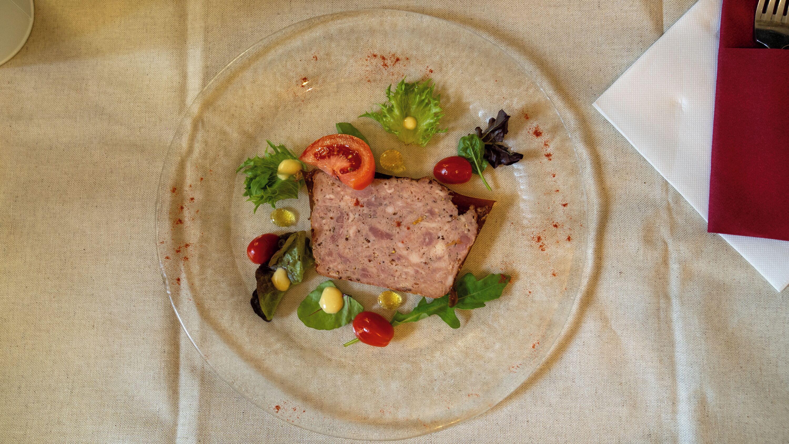 Um prato com uma fatia de carne, tomates cereja, alface e um guardanapo vermelho sobre uma toalha de mesa.