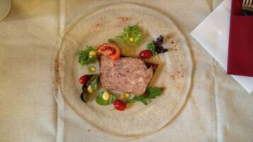Um prato com uma fatia de carne, tomates cereja, alface e um guardanapo vermelho sobre uma toalha de mesa.