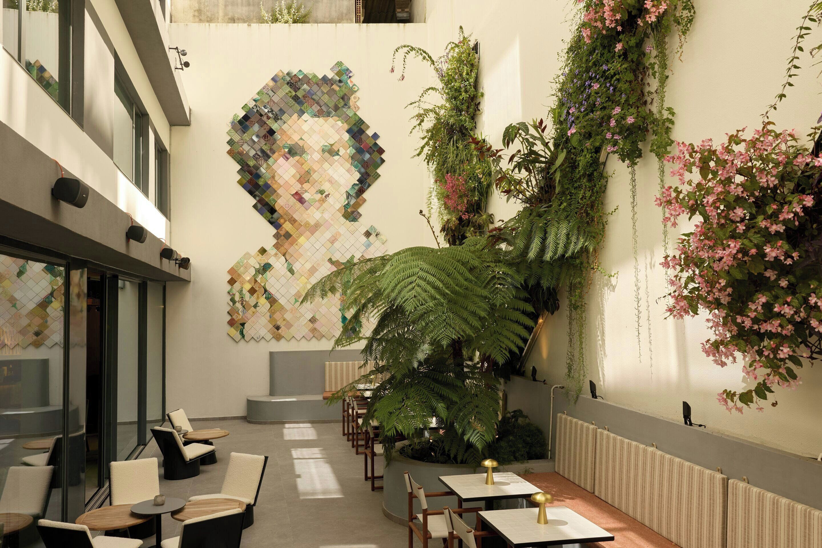 Um interior moderno com uma grande obra de arte em mosaico, plantas de interior e um espaço de estar com mesas e cadeiras.