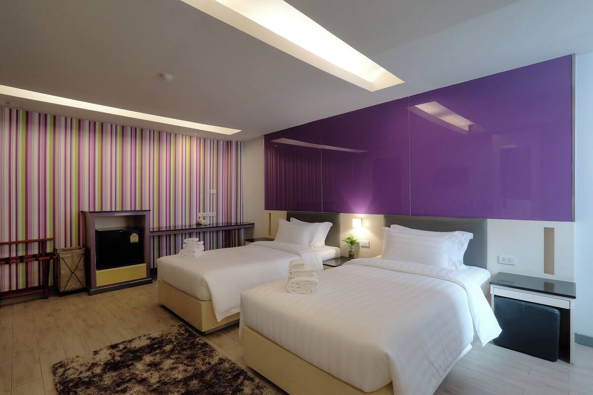 Quarto de hotel moderno com duas camas, um espelho grande e uma parede listrada.