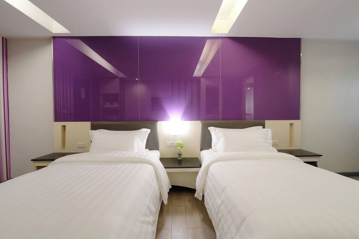 Quarto de hotel com duas camas, um espelho grande e uma mesinha com um vaso.