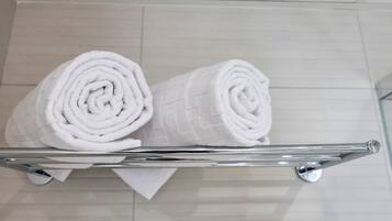 Duas toalhas brancas enroladas em um suporte de toalhas cromado em um banheiro com piso de azulejos.