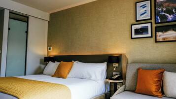 Quarto de hotel com cama, mesa de cabeceira com telefone e sofá.