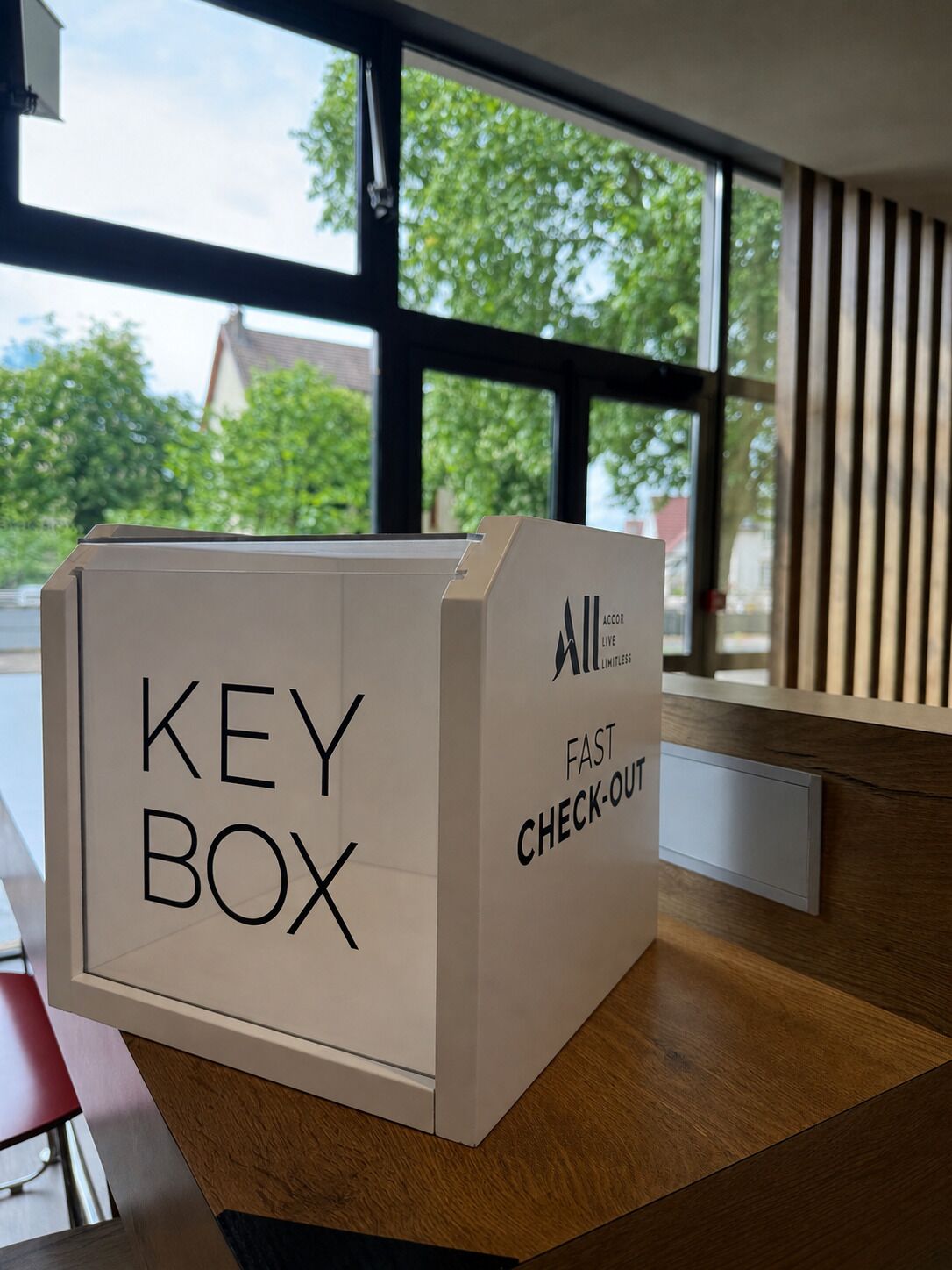Uma caixa para chaves com a etiqueta 'KEY BOX' e 'FAST CHECK-OUT', em um interior moderno com grandes janelas.
