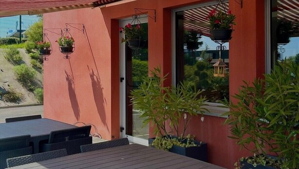 Uma área de estar ao ar livre com toldo listrado em vermelho e branco, móveis de vime e plantas em vasos.