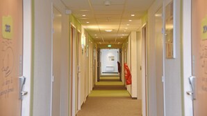Corredor com portas em ambos os lados, carpete verde e teto branco com luzes.