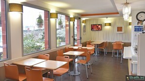 Um restaurante com mesas, cadeiras, janelas amplas e um relógio na parede.