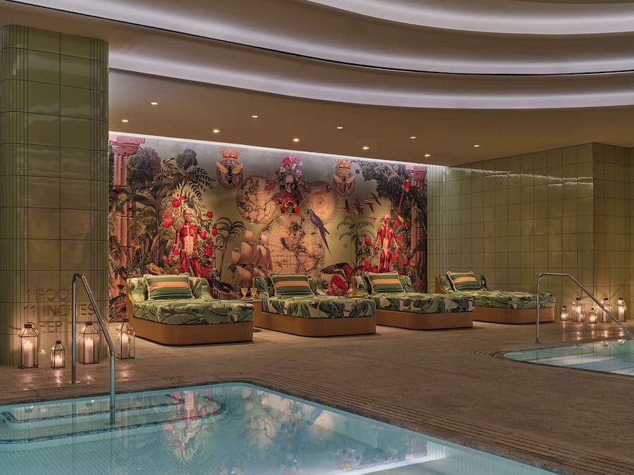 Quarto de hotel com um grande mural, piscina e várias áreas de estar.
