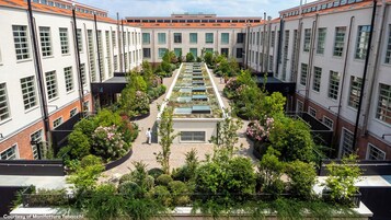 Um pátio com jardim central, rodeado por edifícios com grandes janelas e telhado em azulejos.