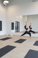 Um estúdio de yoga com um espelho grande, tapetes de yoga pretos e chão de madeira.