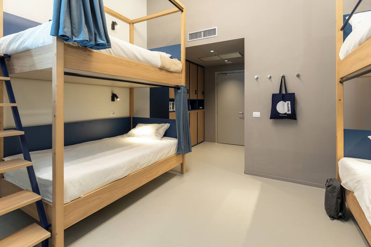 Quarto com beliche, escrivaninha e uma mochila pendurada na parede.