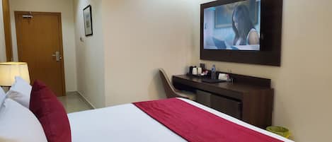 Quarto de hotel com cama, escrivaninha, televisão fixada na parede e uma porta.