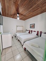 Quarto de hotel com duas camas de solteiro, uma pequena mesa, um ventilador de teto e piso de azulejos.
