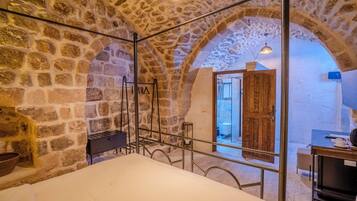 Um quarto rústico com paredes de pedra, uma cama, uma porta de madeira e uma pequena mesa com xícara e pires.