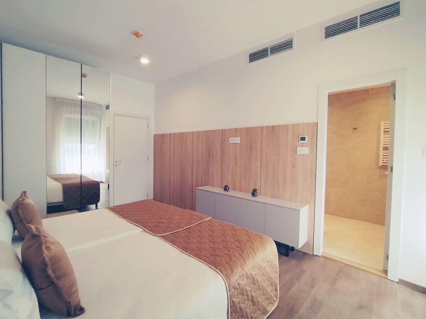 Quarto moderno com uma cama grande, painel de parede de madeira, mesa de cabeceira e guarda-roupa.