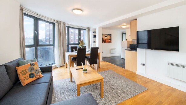 Uma sala de estar moderna com um sofá, uma mesa de jantar e uma TV fixada na parede.