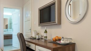 Quarto de hotel com secretária de madeira, televisão, espelho e uma cesta de frutas.