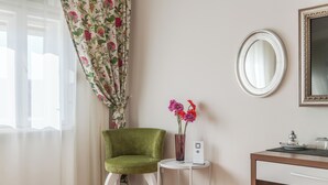 Quarto com uma cadeira verde, uma mesinha com um vaso de flores, um espelho e um armário.