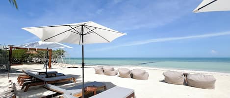 Na praia, areia branca, espreguiçadeiras, guarda-sóis