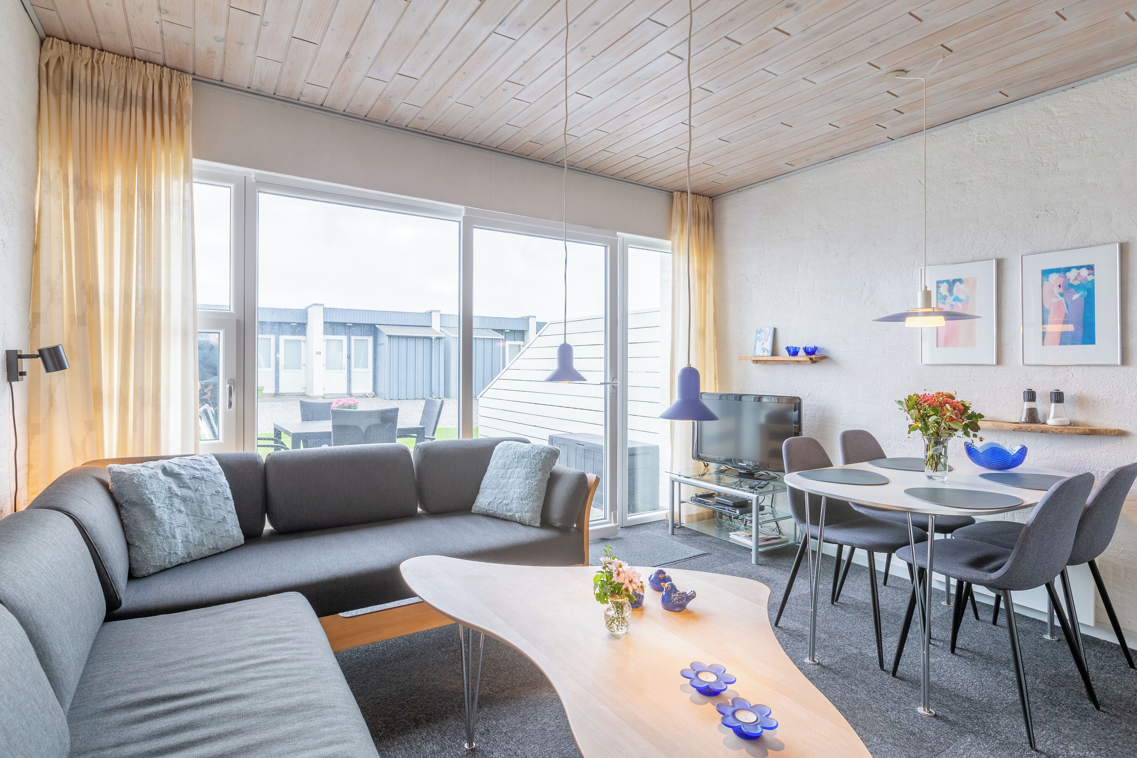 Uma sala de estar moderna com um sofá cinzento, uma mesa de centro de madeira e uma área de jantar com uma mesa redonda e cadeiras.