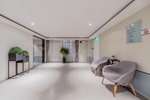 Uma área de espera moderna com balcão de recepção, duas cadeiras cinzas, um vaso de plantas e uma placa na parede.