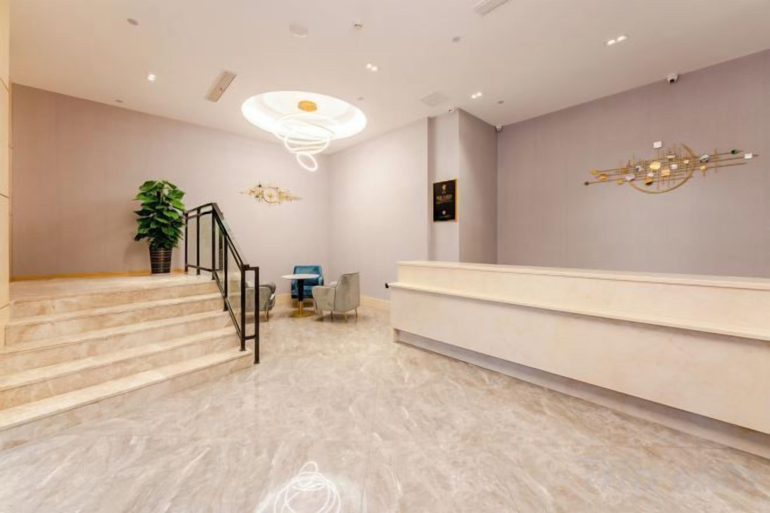Uma área de recepção com piso de mármore, balcão de atendimento, escada e luminária fixada na parede.