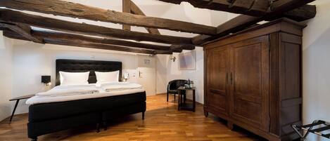 Quarto com teto de madeira, cama, guarda-roupa e uma pequena mesa.