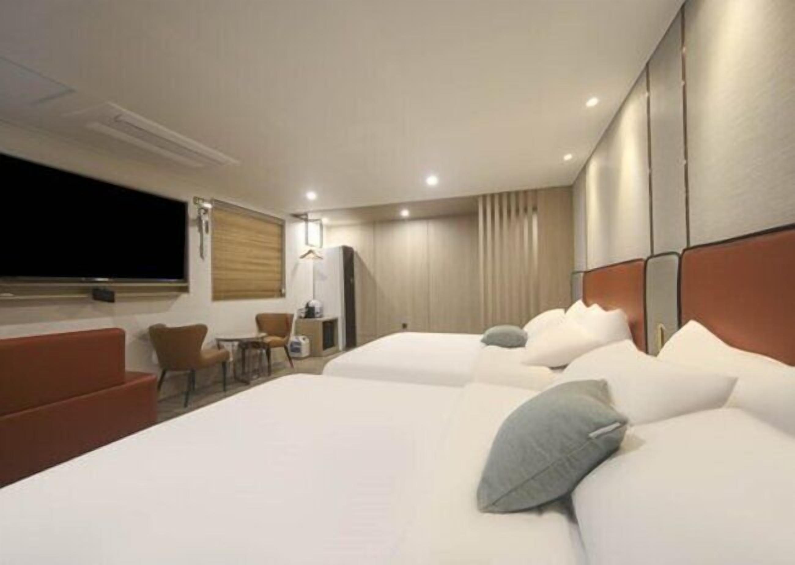 Quarto de hotel com duas camas, televisão, escrivaninha e uma cadeira.