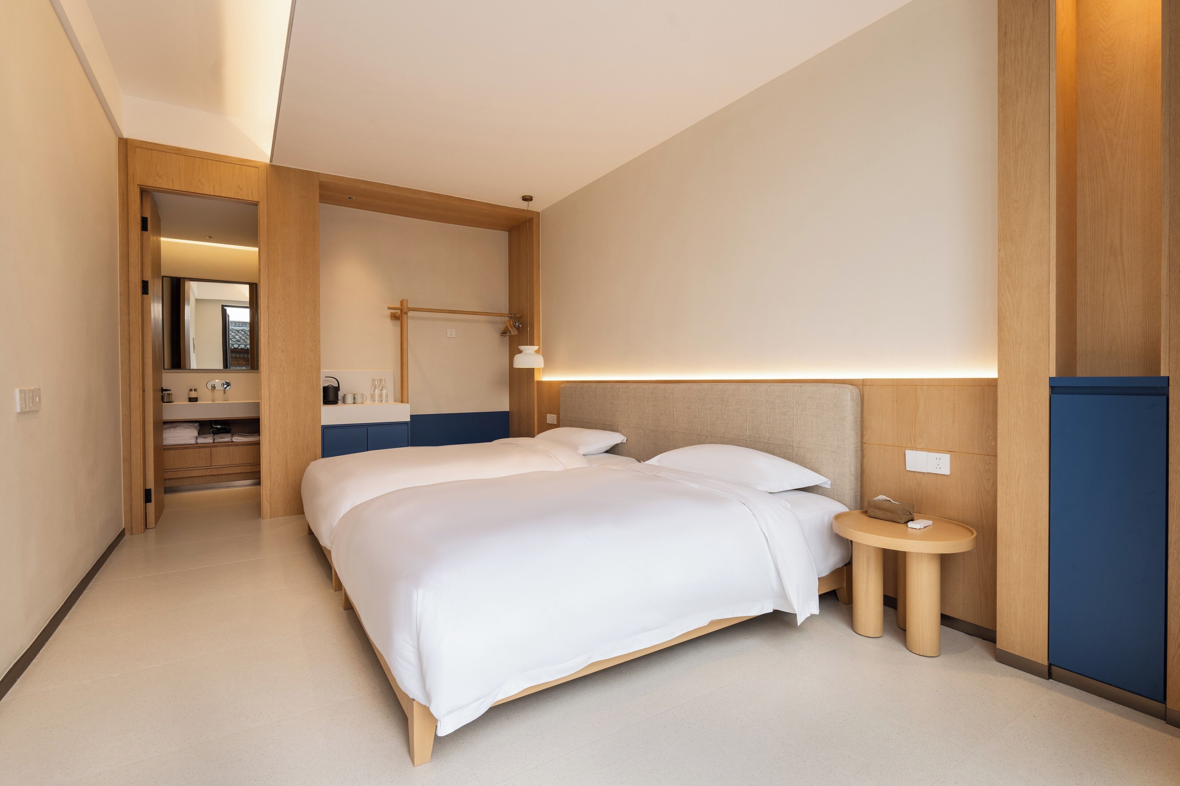 Quarto de hotel moderno com uma cama grande, mesas de cabeceira, um espelho e um guarda-roupa de madeira.