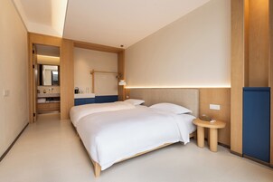 Quarto de hotel moderno com uma cama grande, mesas de cabeceira, um espelho e um guarda-roupa de madeira.