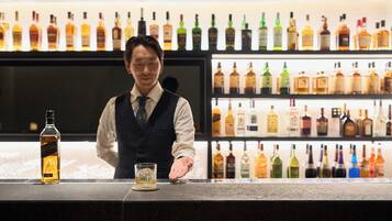 Um bartender num bar, com várias garrafas de bebidas alcoólicas ao fundo.