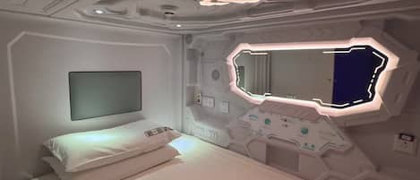 Quarto com cama, televisão na parede e um espelho hexagonal exclusivo com iluminação integrada.