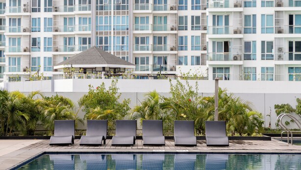 Piscina com espreguiçadeiras e um edifício ao fundo com várias varandas.