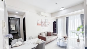 Uma sala de estar moderna com área de jantar, um sofá, uma mesa de centro e uma janela grande com cortinas.