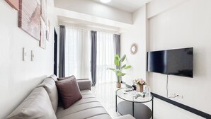 Uma sala de estar moderna com sofá, mesa de centro redonda, TV de tela plana na parede e uma janela grande com cortinas.