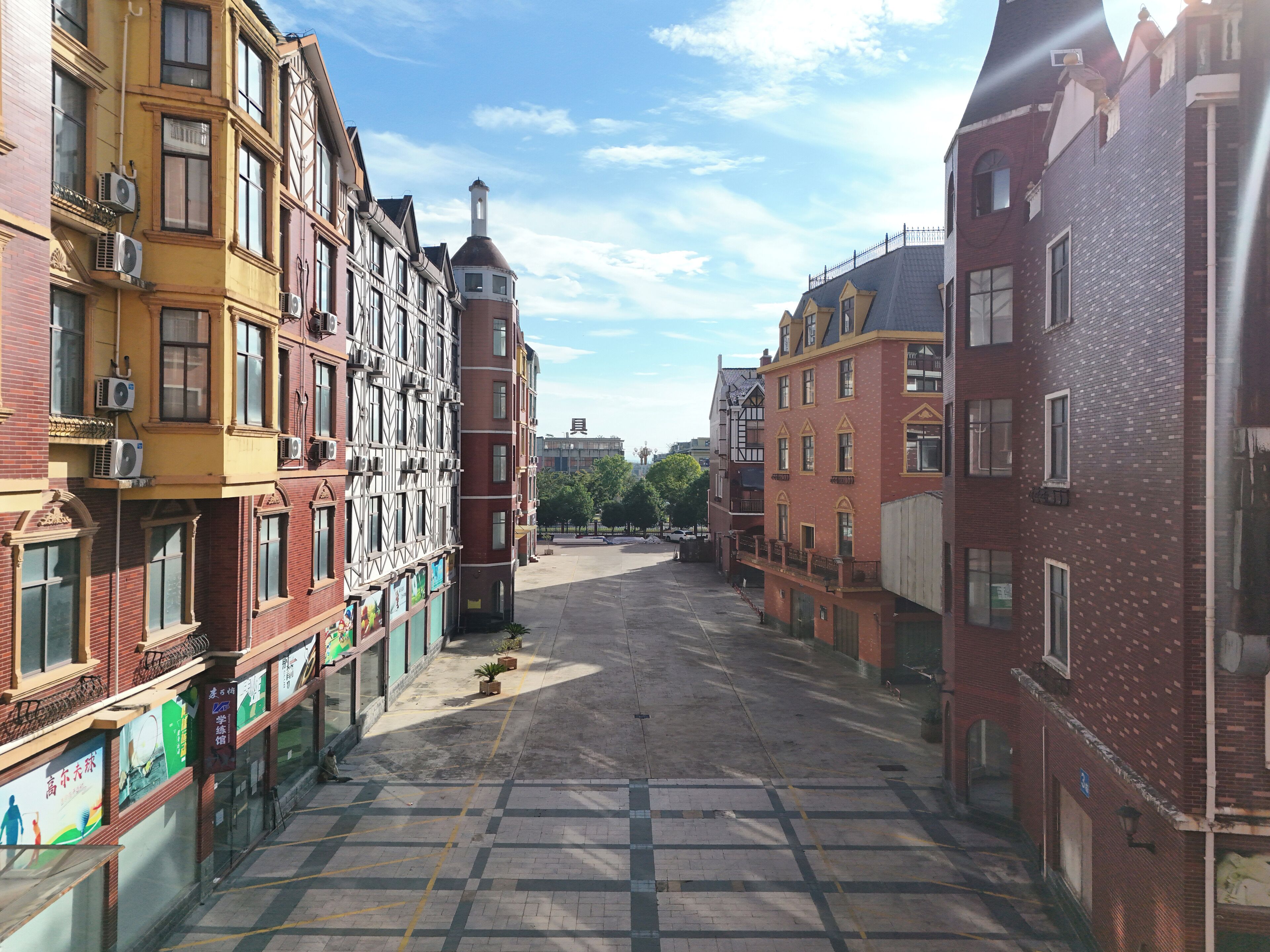 Vista da rua com edifícios altos, céu claro e um prédio distante.